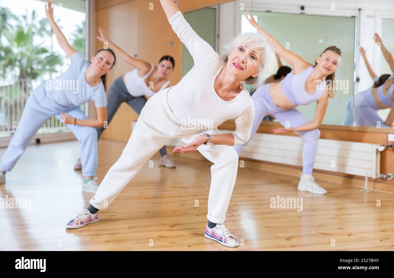 Mature female coach dancing and practicing new movements with group of ...