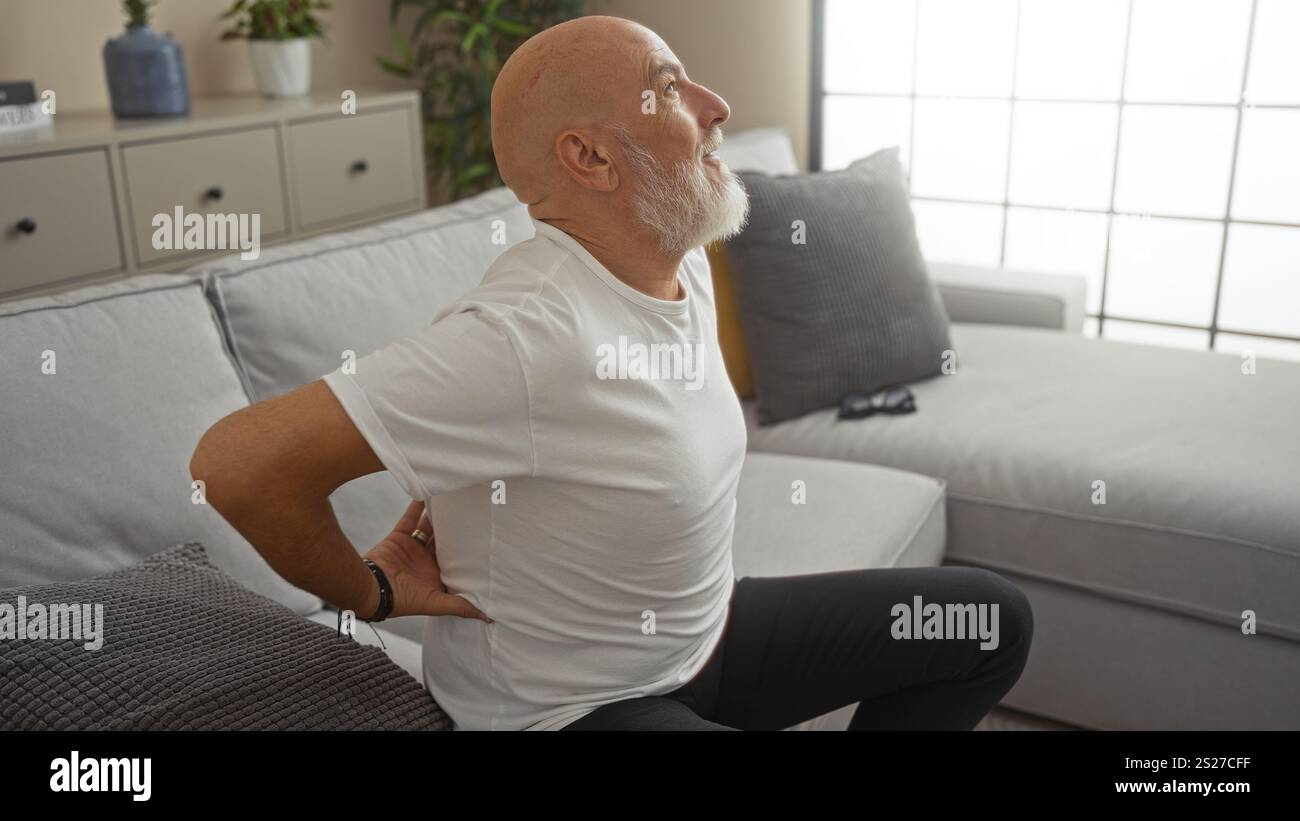 Man with grey hair and beard sitting in modern living room holds his ...