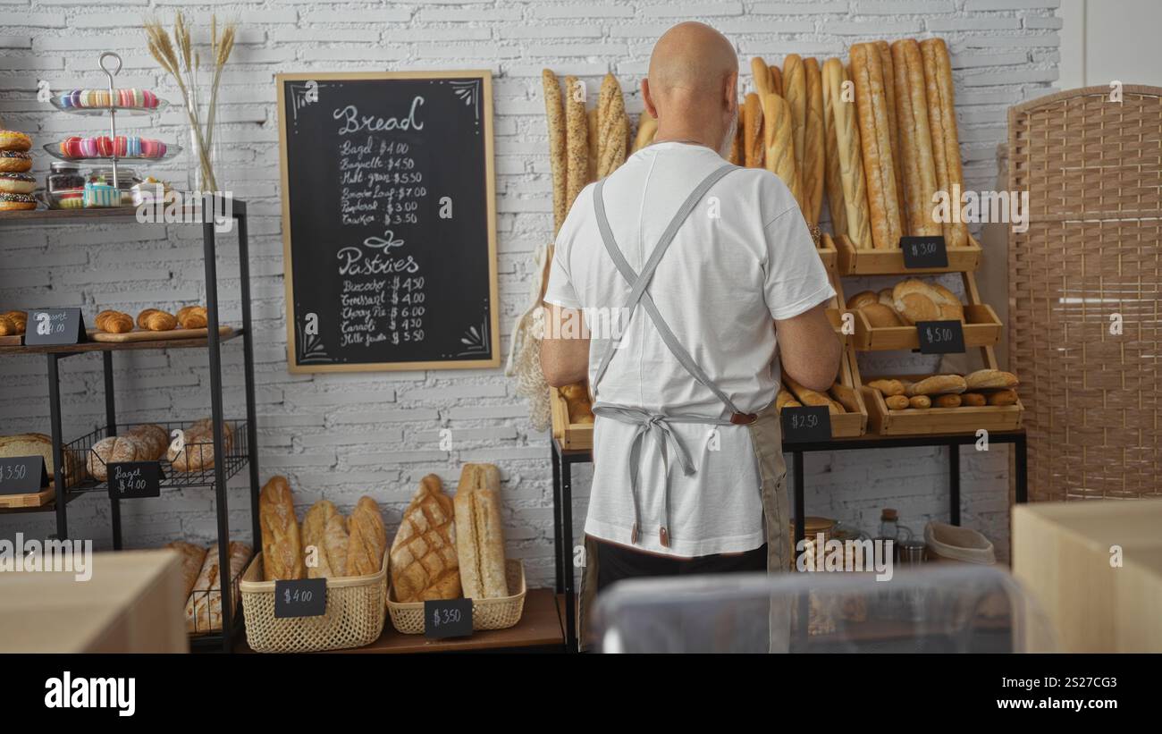 Mature man with bald head in bakery facing bread display, wearing apron ...