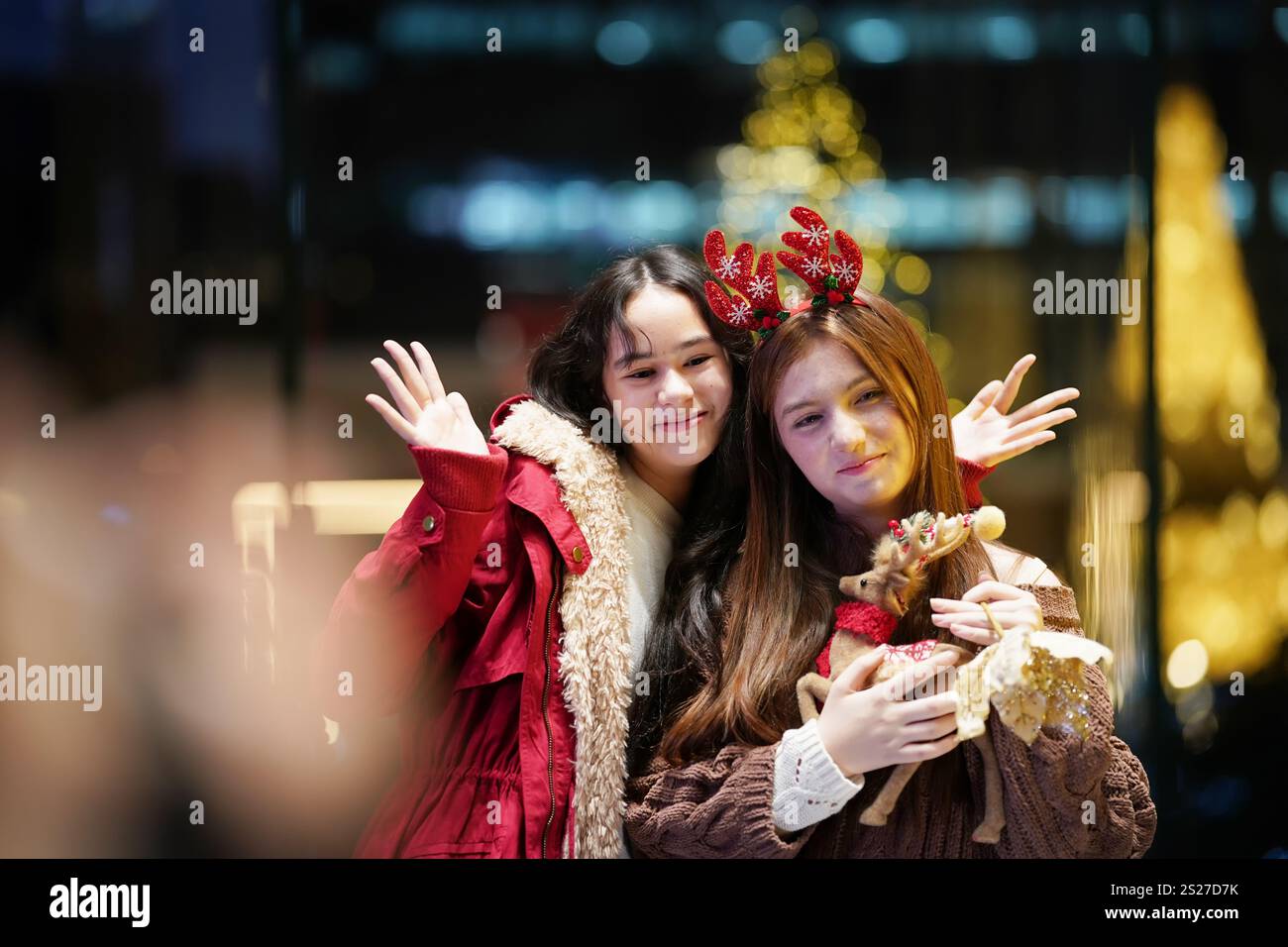 Two young women pose joyfully in festive outfits, one holding a ...