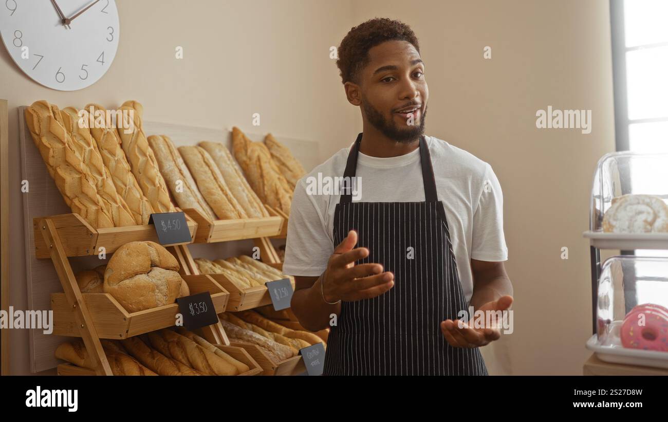 Young man in bakery wearing apron explaining products with shelves of ...