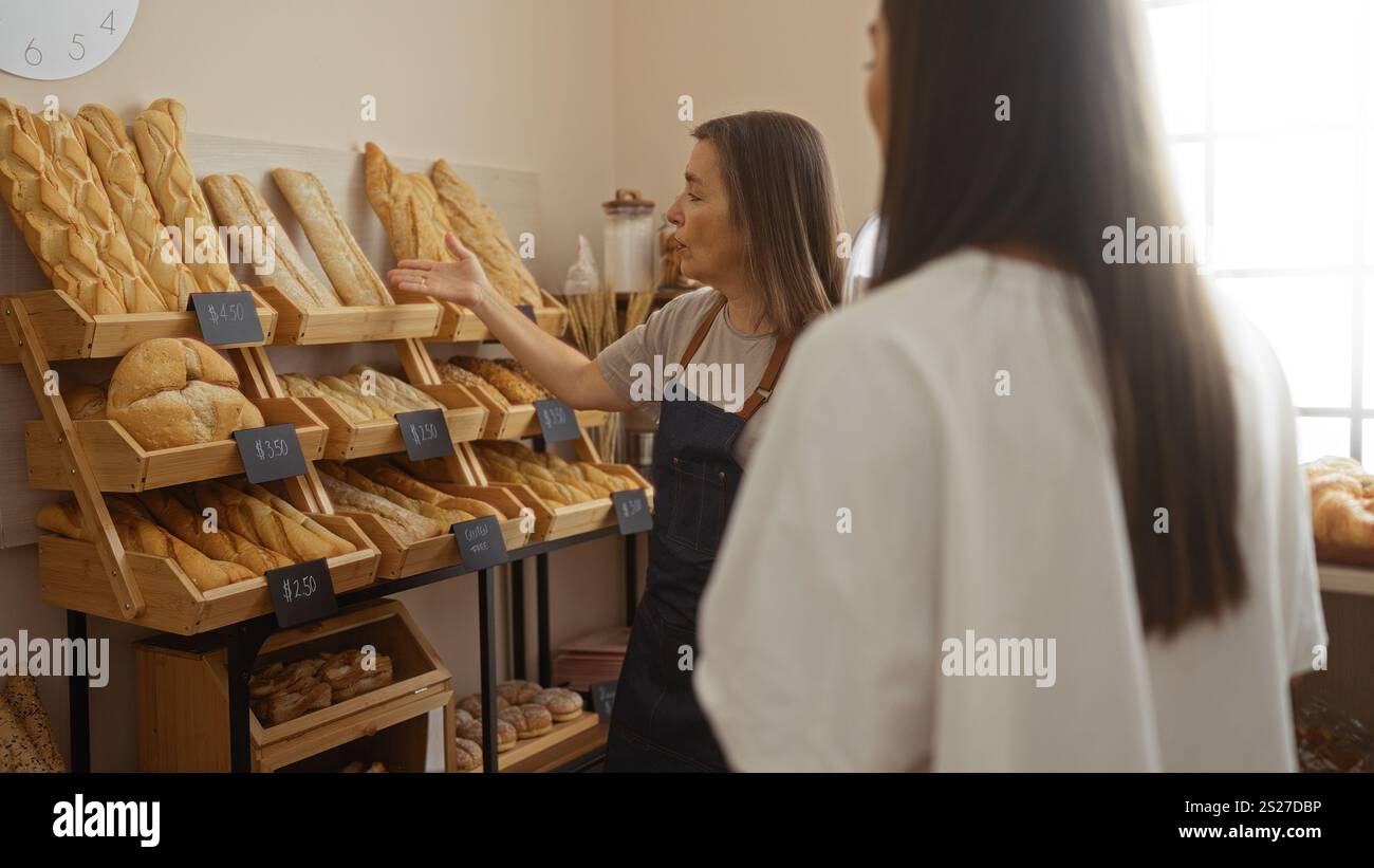 Female baker talking with a female customer inside a bakery, pointing ...