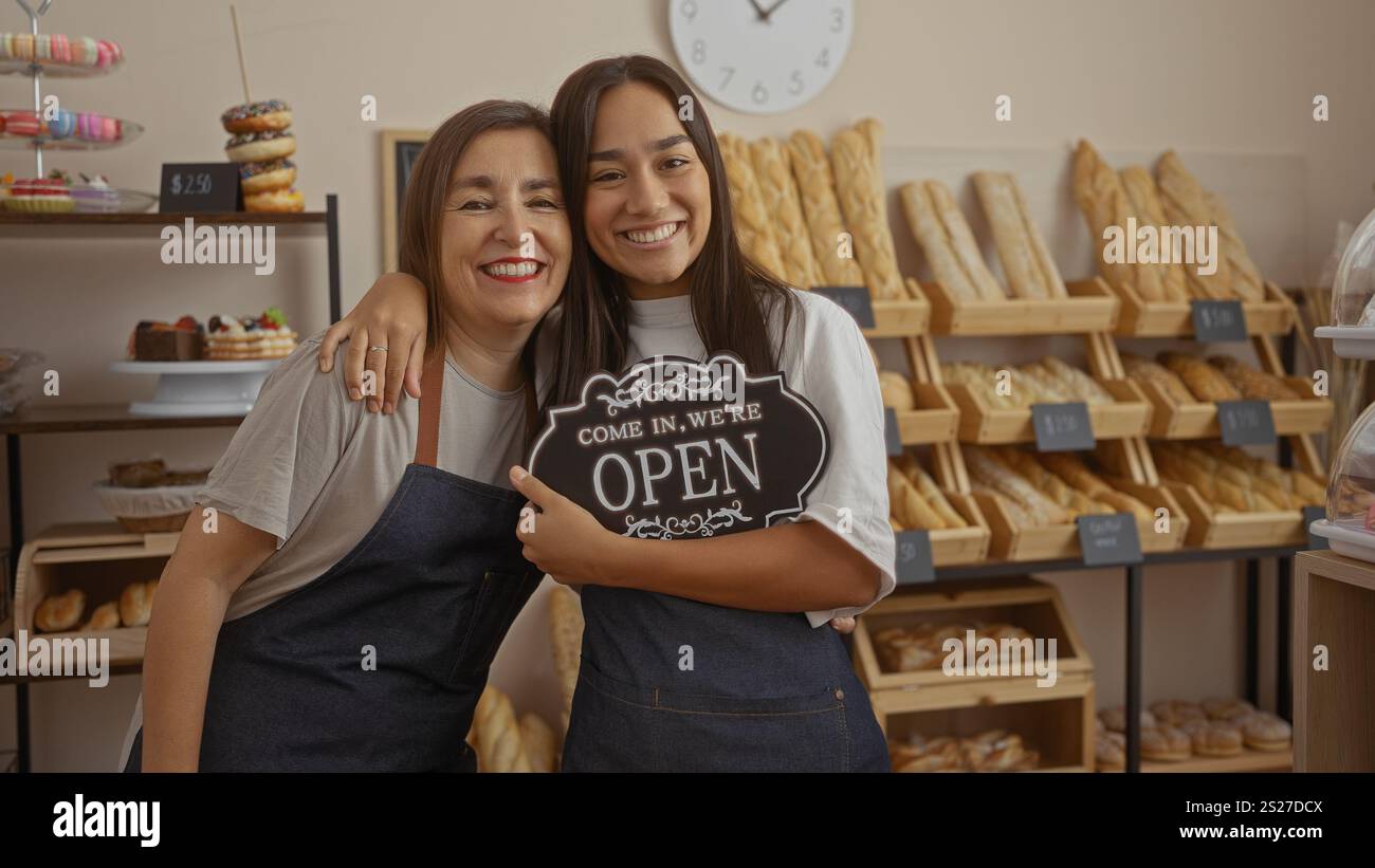 Two smiling women bakers standing together in a bakery shop holding an ...
