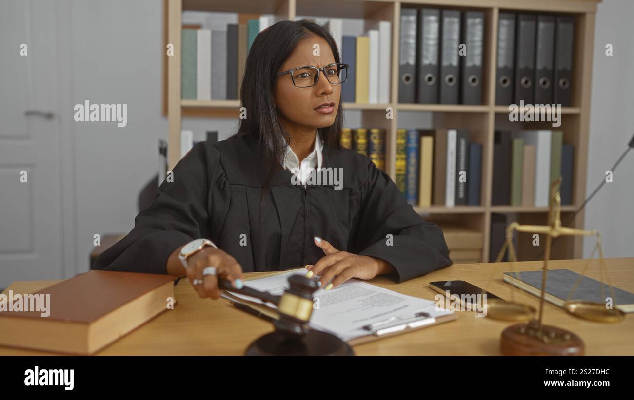 Young female judge in black robe with gavel at indoor office with books ...