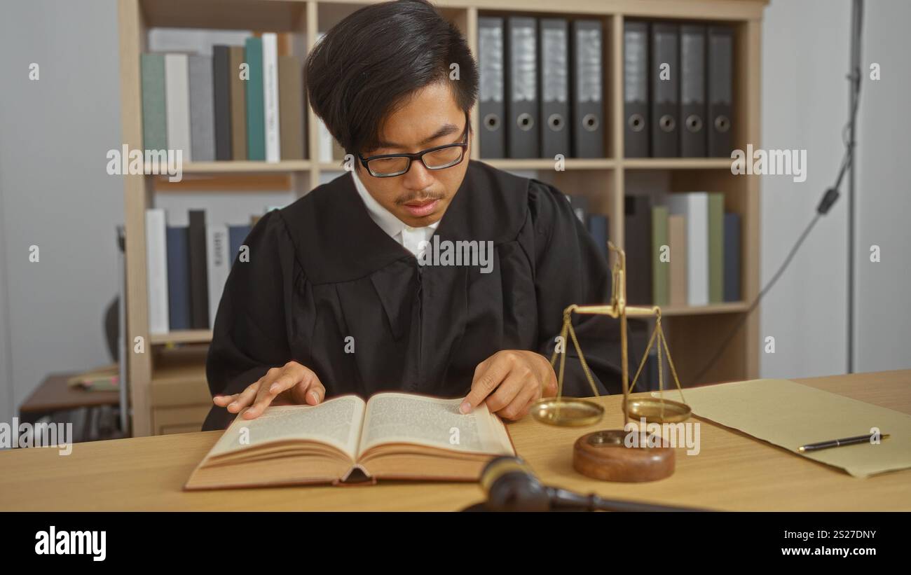 Young asian man in a judge's robe reading a book in an office courtroom ...