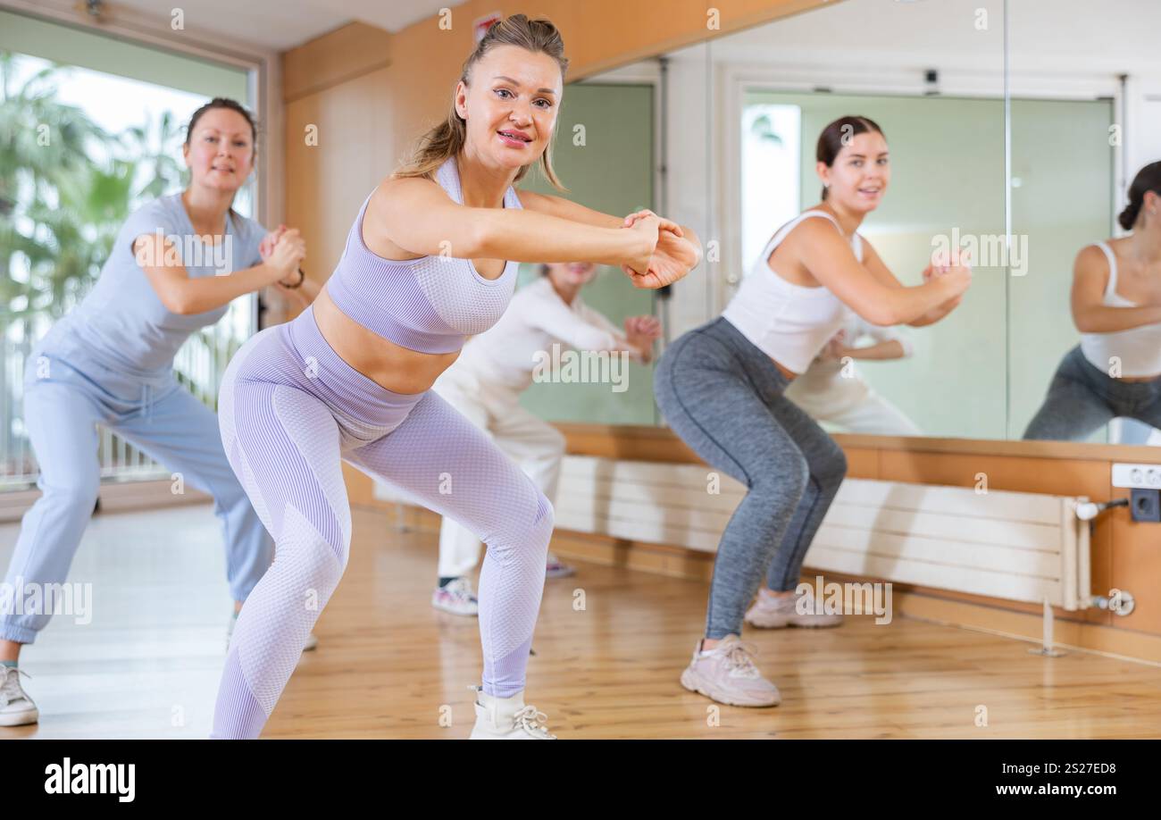 Smiling active women of different ages making squats during dancing ...