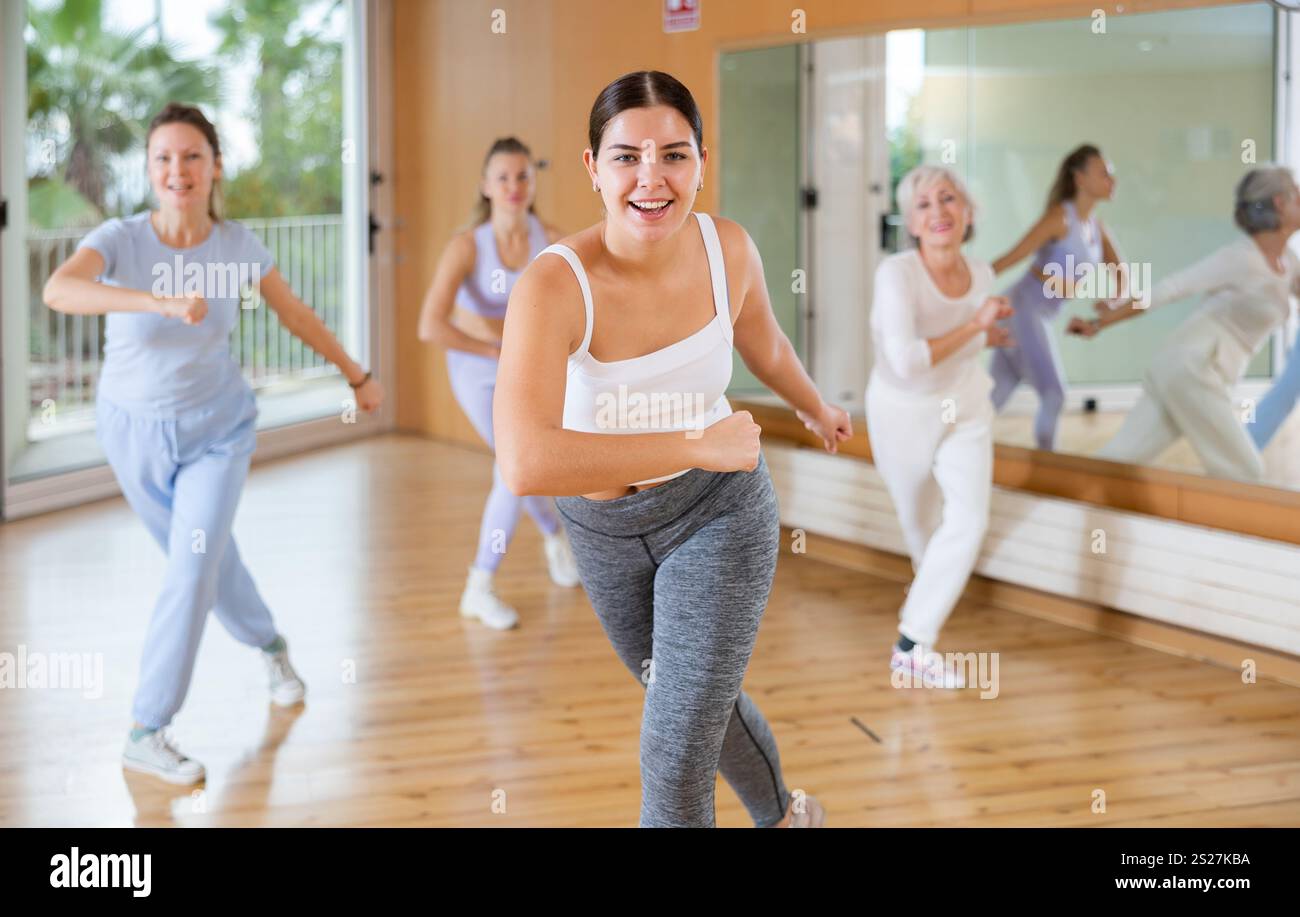Excited positive women of different ages performing modern dancing exercises in school for ...