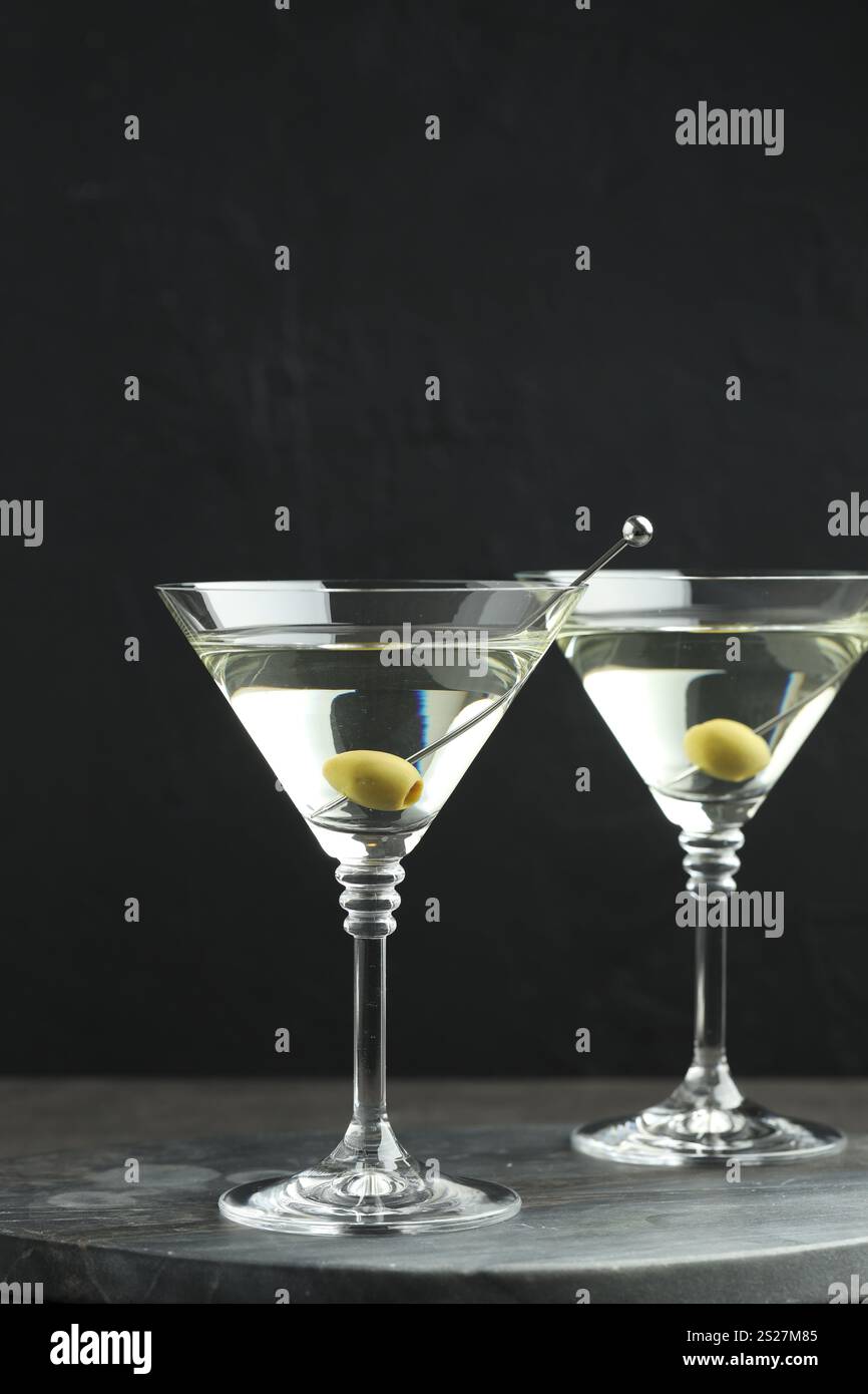 Martini cocktail with olives in glasses on grey table against black ...