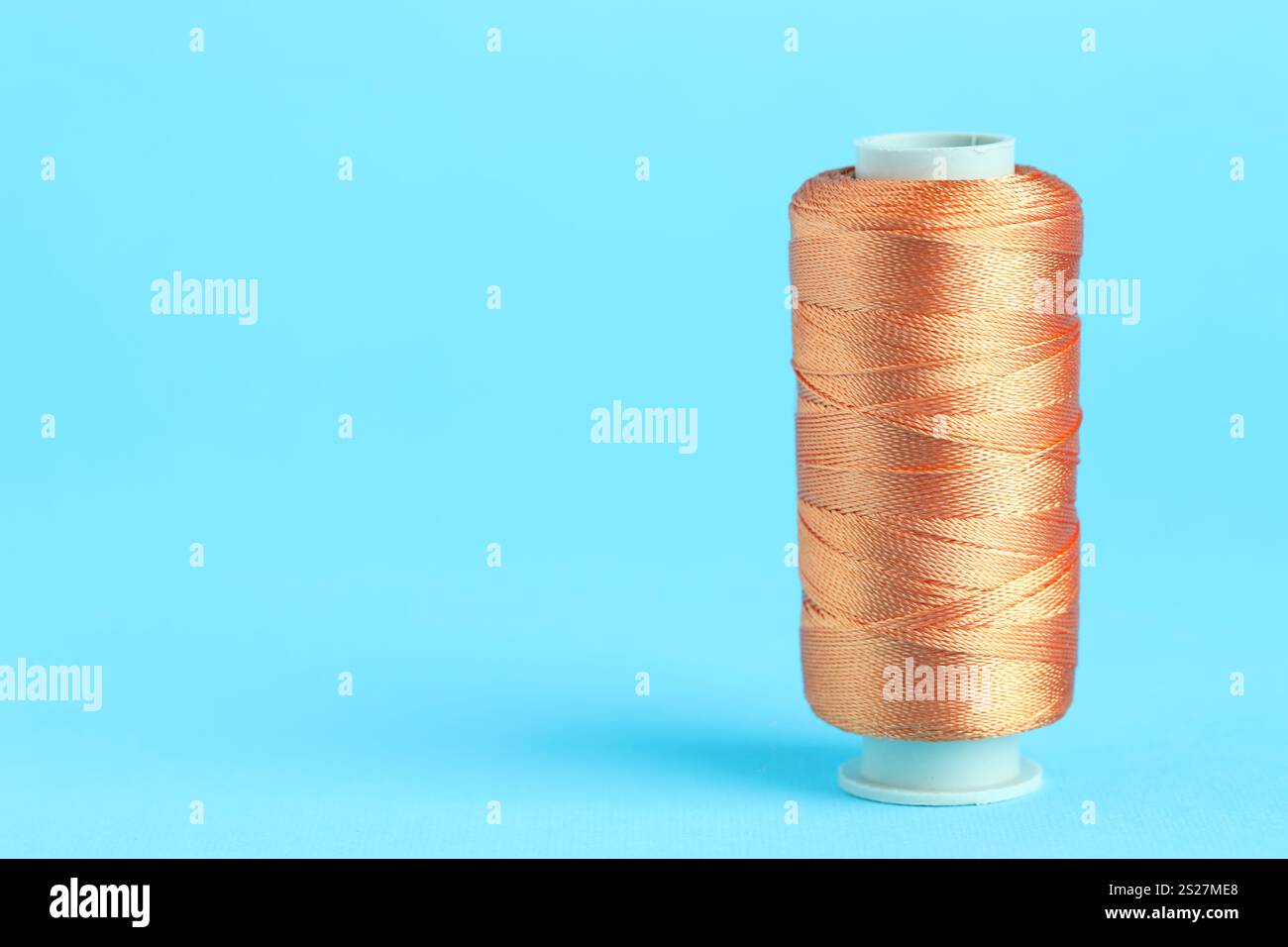Spool of orange sewing thread on light blue background, space for text ...