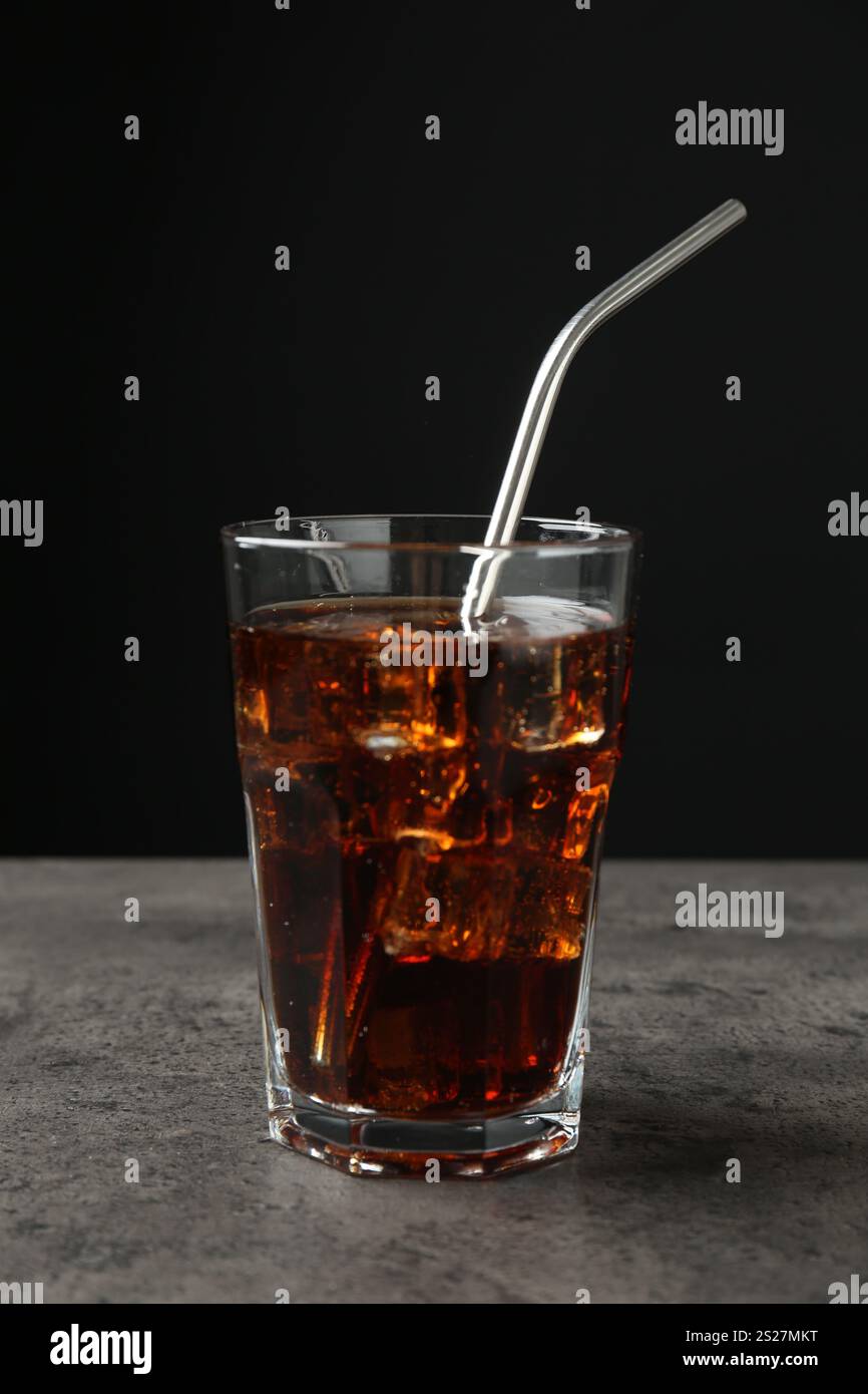Cold cola with ice cubes and drinking straw in glass on grey table ...