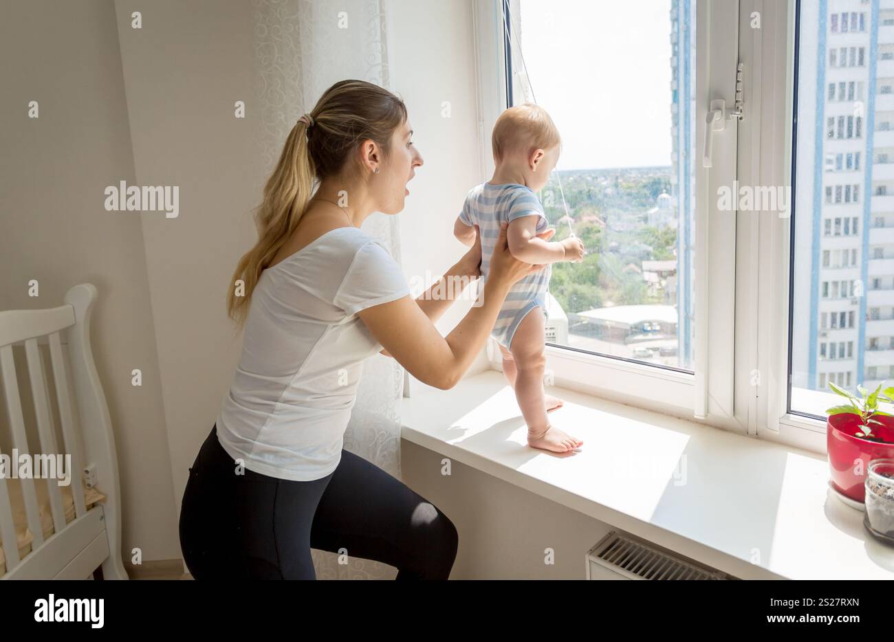 Mother rushing to her baby that is trying to open window Stock Photo ...