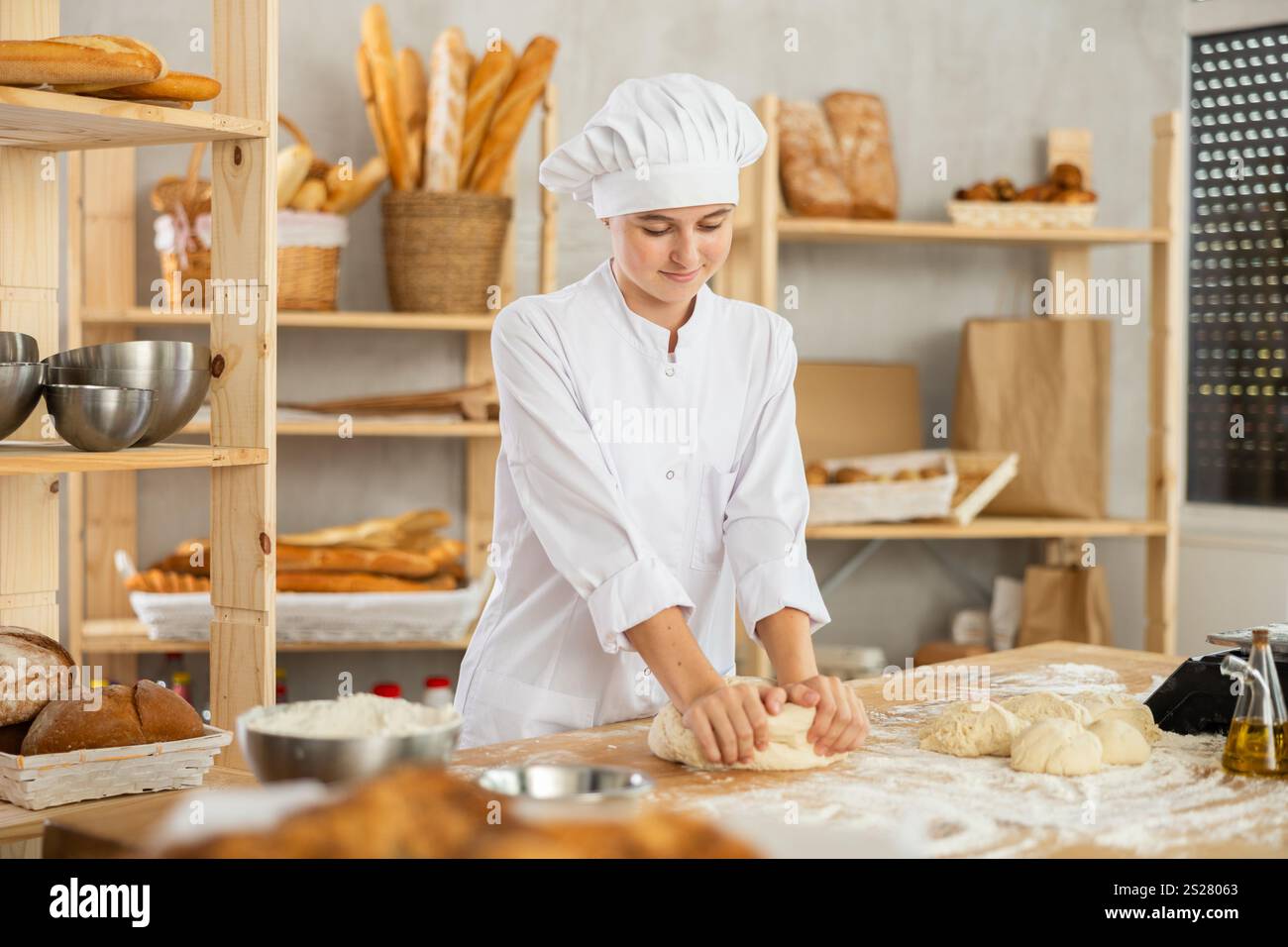 Teen girl works in bakery as baker, kneads dough, works with flour ...