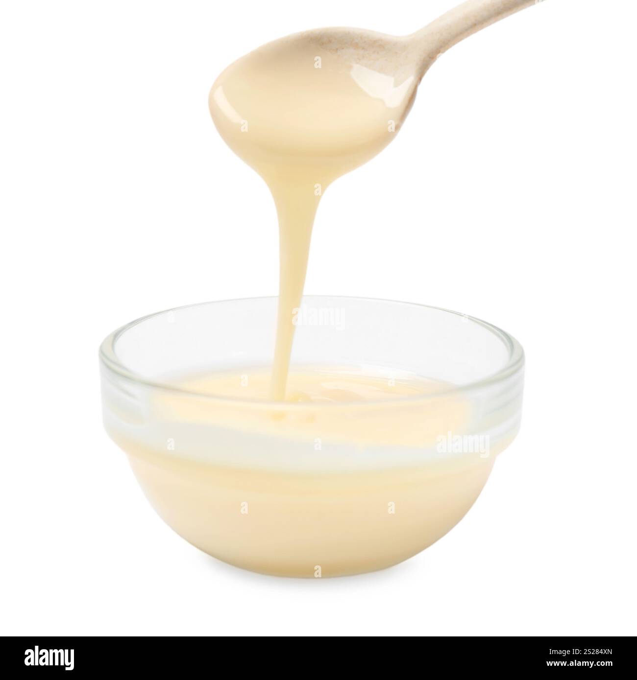Condensed milk flowing down from spoon into bowl isolated on white ...