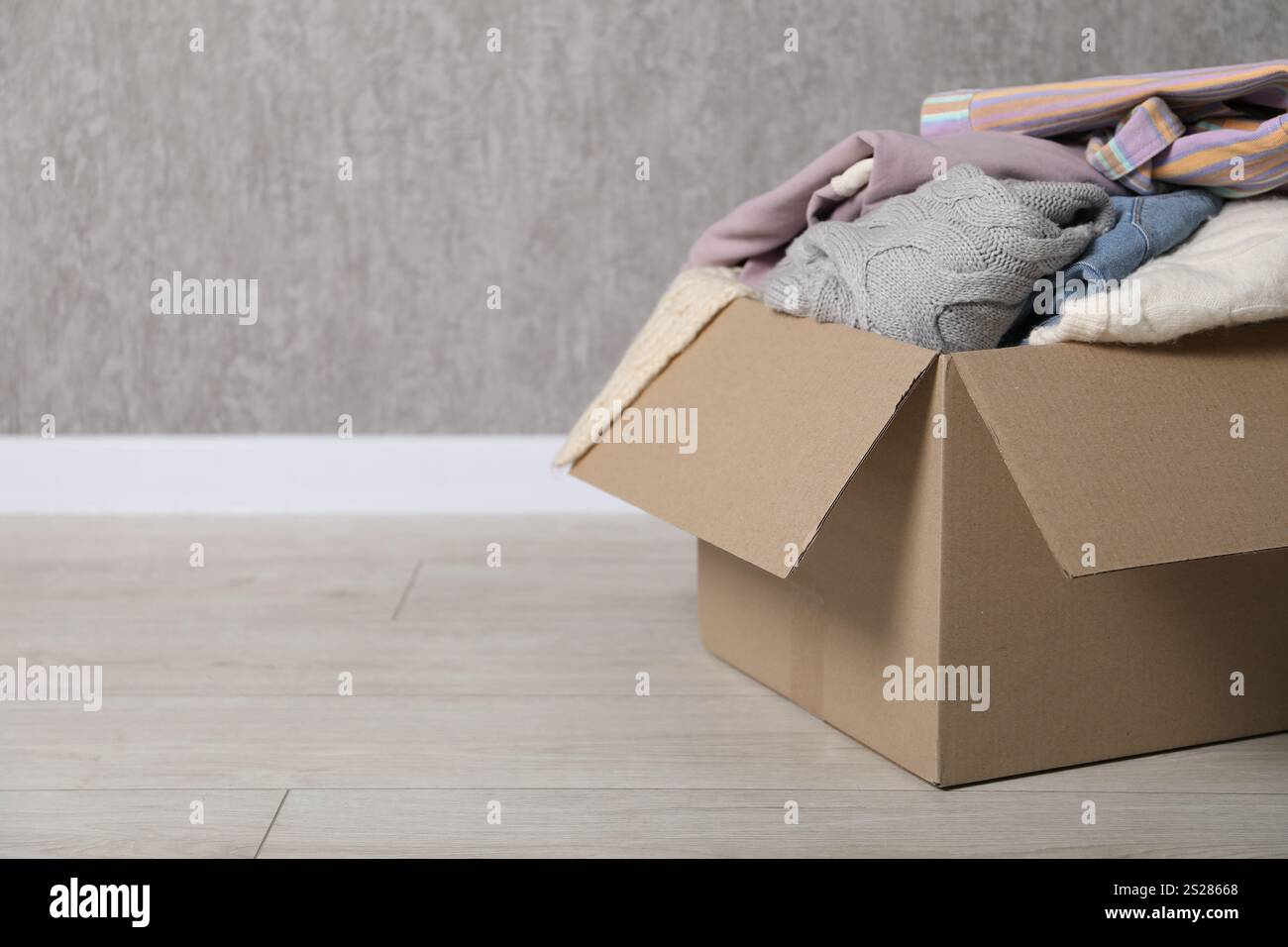 Used clothes in cardboard box on floor near grey wall. Space for text ...