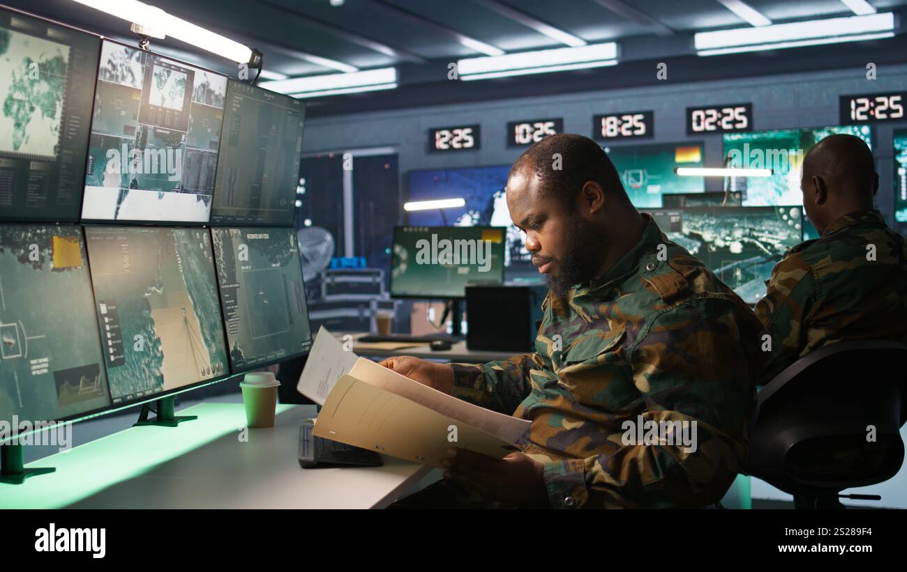 Military soldier in mission control center overseeing national safety operations, reading folder ...