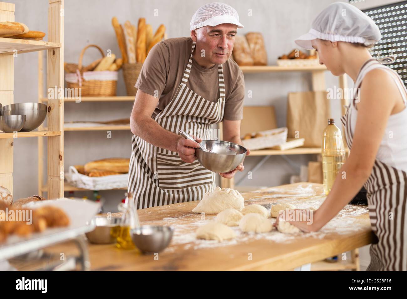 Male baker teaches teenage girl assistant how to make dough Stock Photo ...