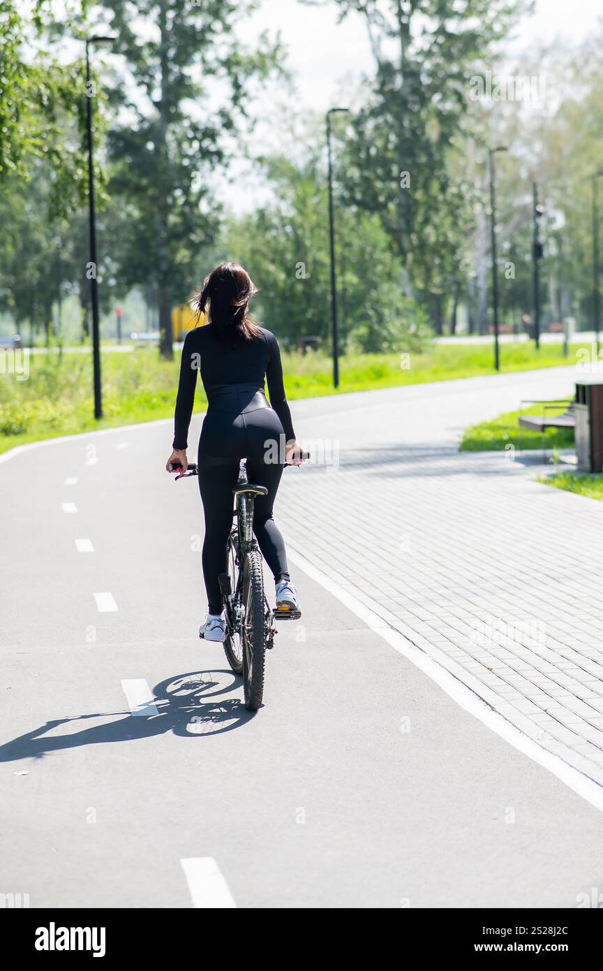 Rear view of Caucasian woman riding bike in park. Vertical photo Stock ...