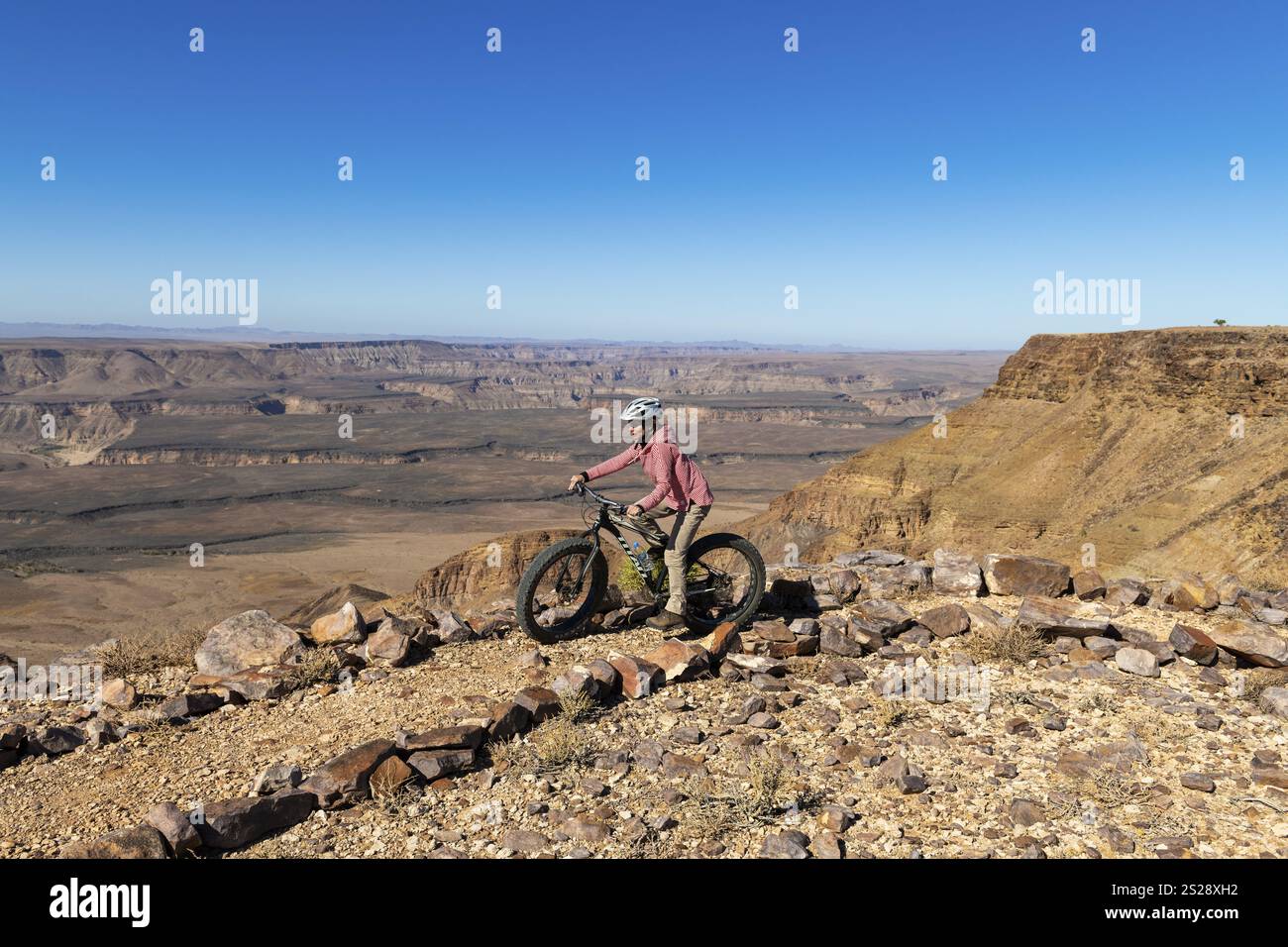 Woman riding a mountain bike, fatbike, on the edge of the abyss, behind ...