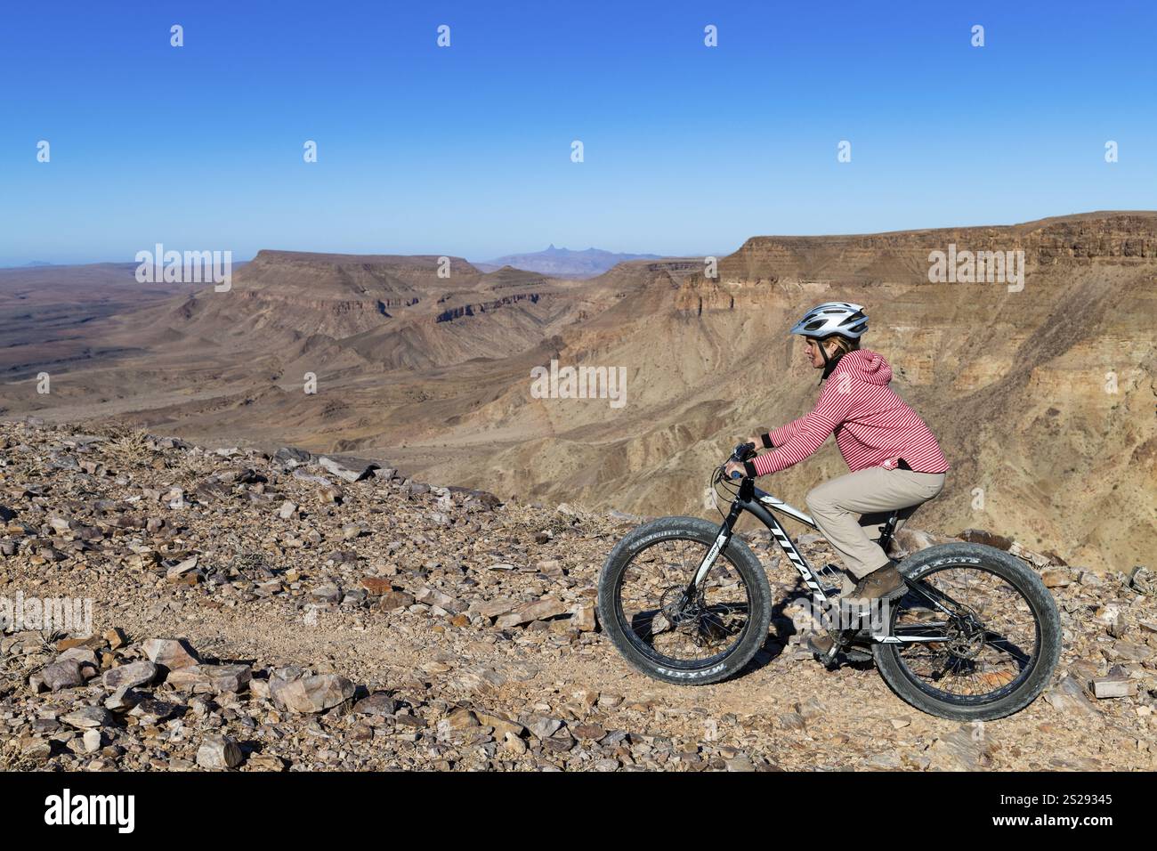 Woman riding a mountain bike, fatbike, on the edge of the abyss, behind the gorge landscape of ...
