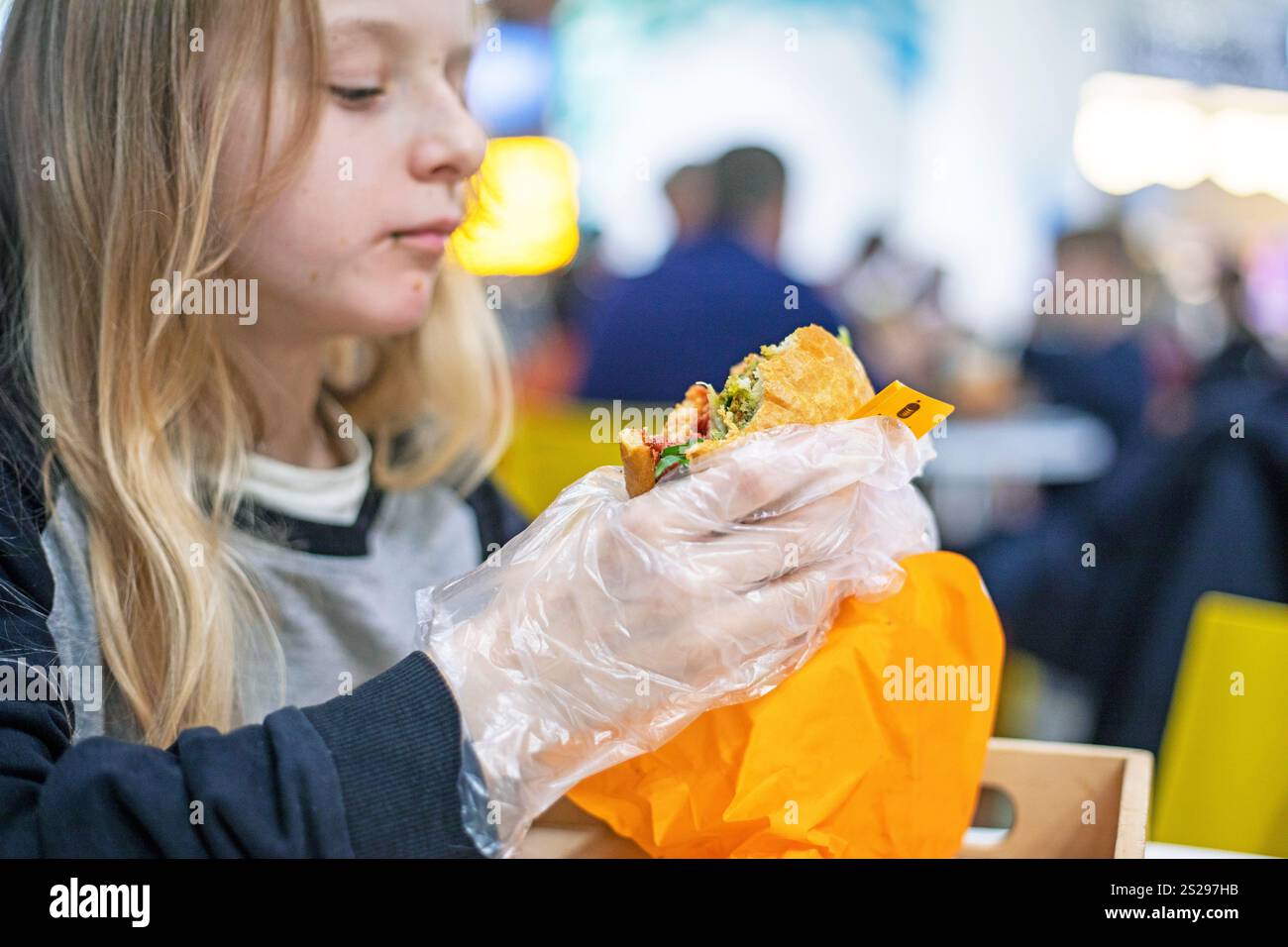 schoolgirl eats a cheeseburger in gloves during recess. school snack ...