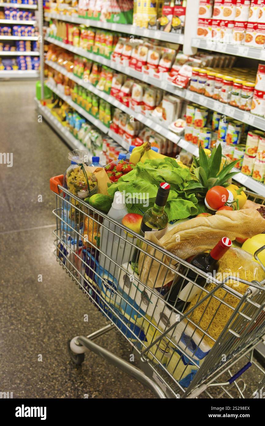 A shopping trolley stands between the shelves in a supermarket aisle ...