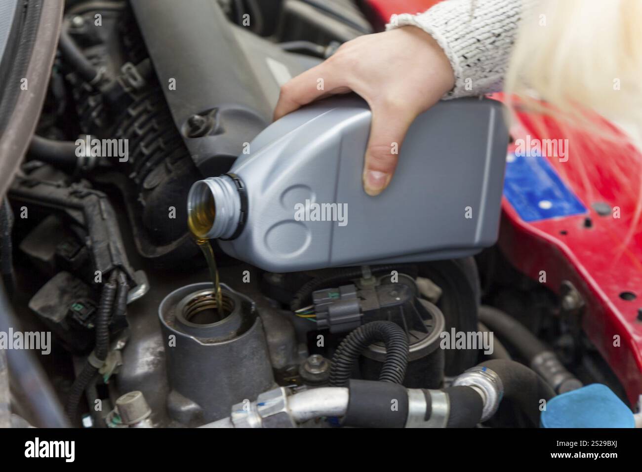 A young woman tops up the oil in her car. Safe driving with the right ...