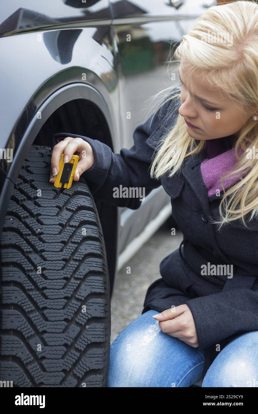 A young woman measures the tread depth of her car tyre. The right depth ...