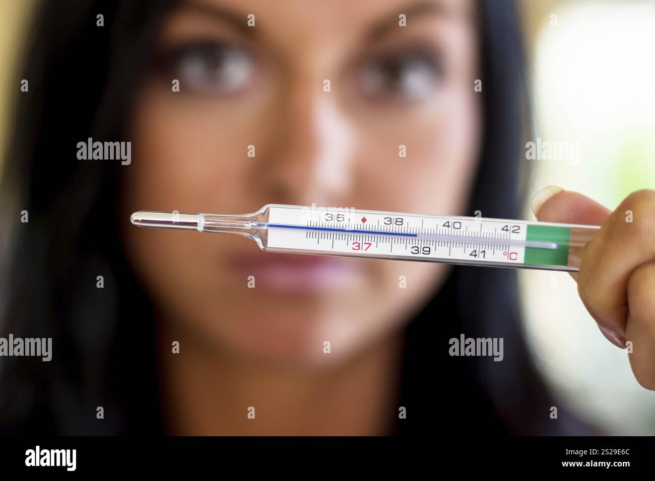 A woman holds a clinical thermometer behind her hand. Symbol photo for ...