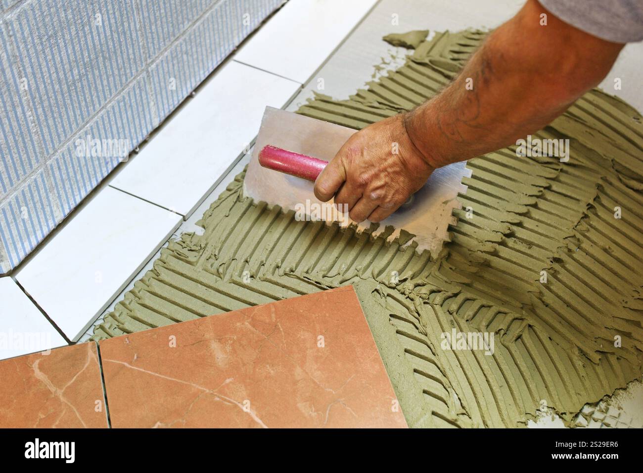 A tiler at work. Gluing floor tiles with tile adhesive and trowel ...