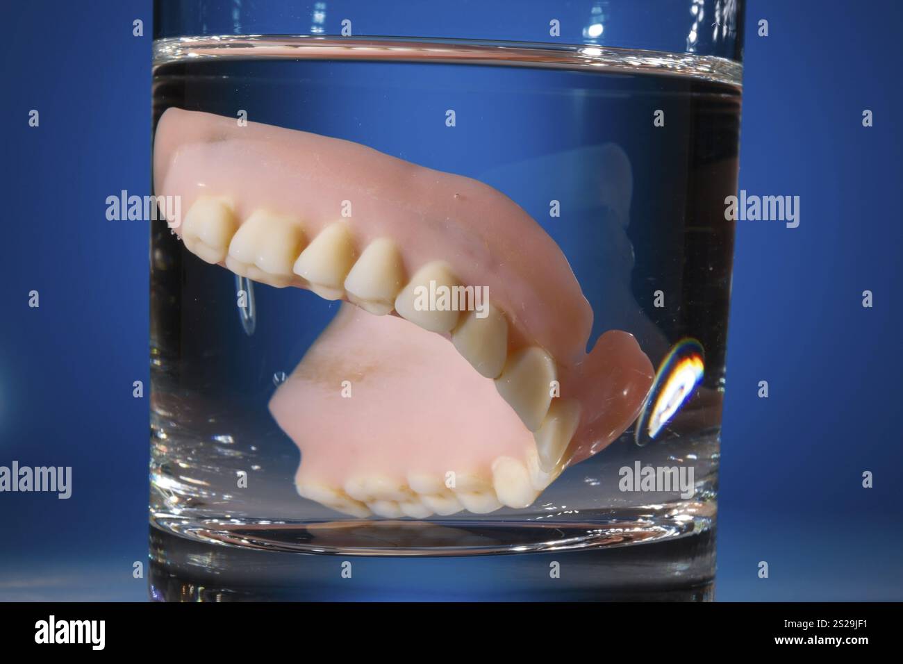 A dental prosthesis is cleaned in a glass of water. Proper hygiene ...