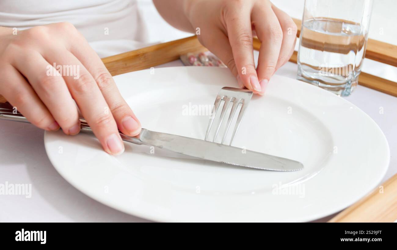 Closeup image of sick woman lying in bed holding fork and knife over ...