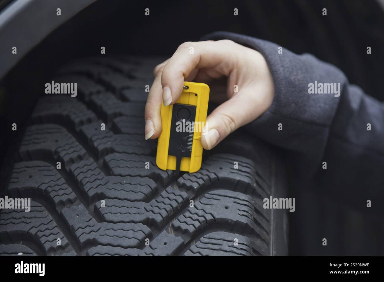 A young woman measures the tread depth of her car tyre. The right depth ...
