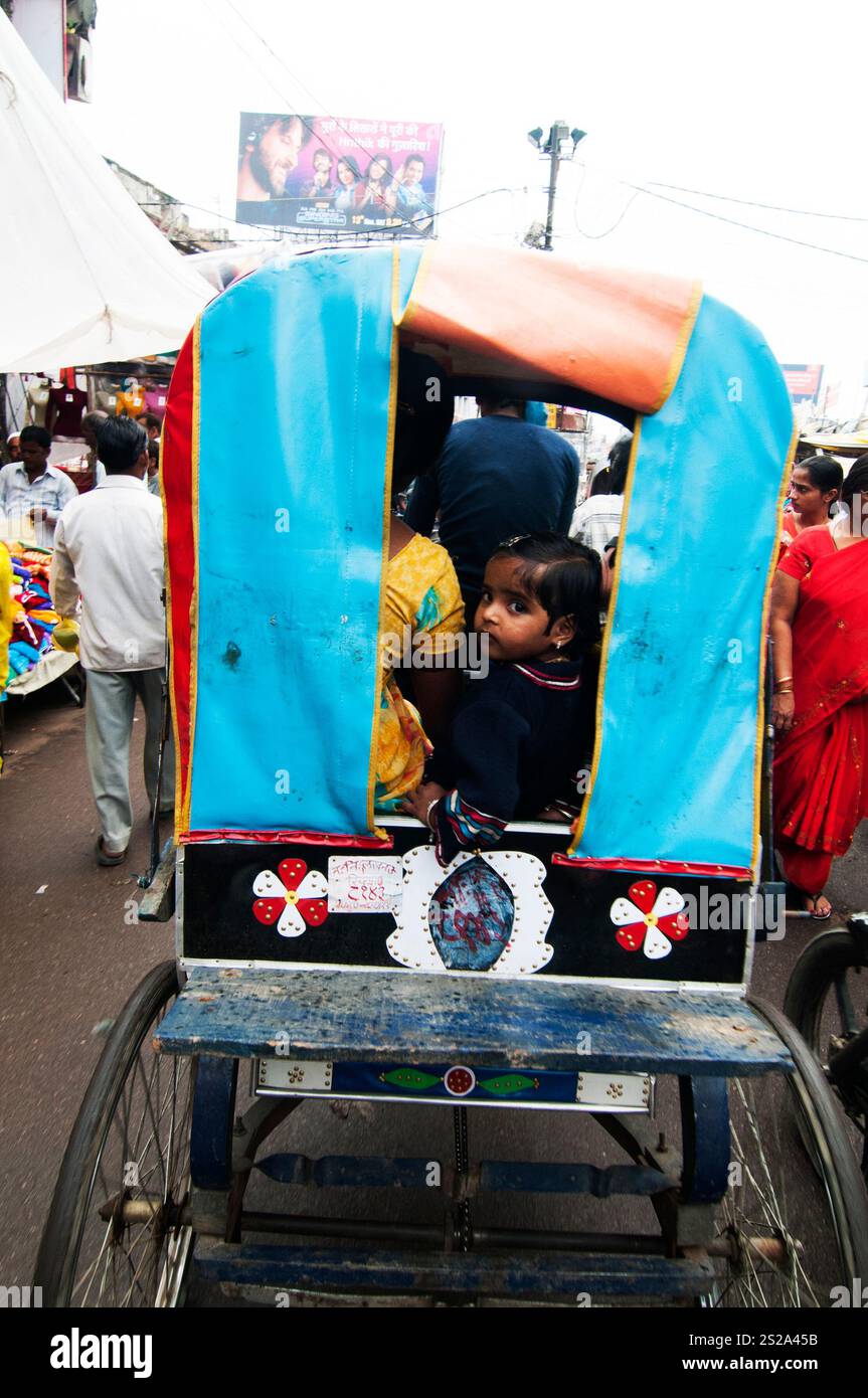 A little girl looking back from the bicycle rickshaw in the market in ...
