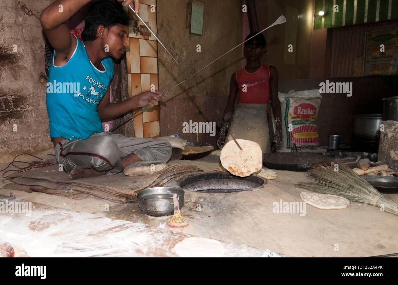 A Man baking roti breads in a tandoor oven in a small bakery at the ...