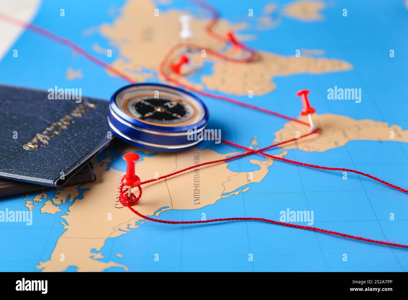 Paper pins with thread, compass and passports on world map, closeup ...