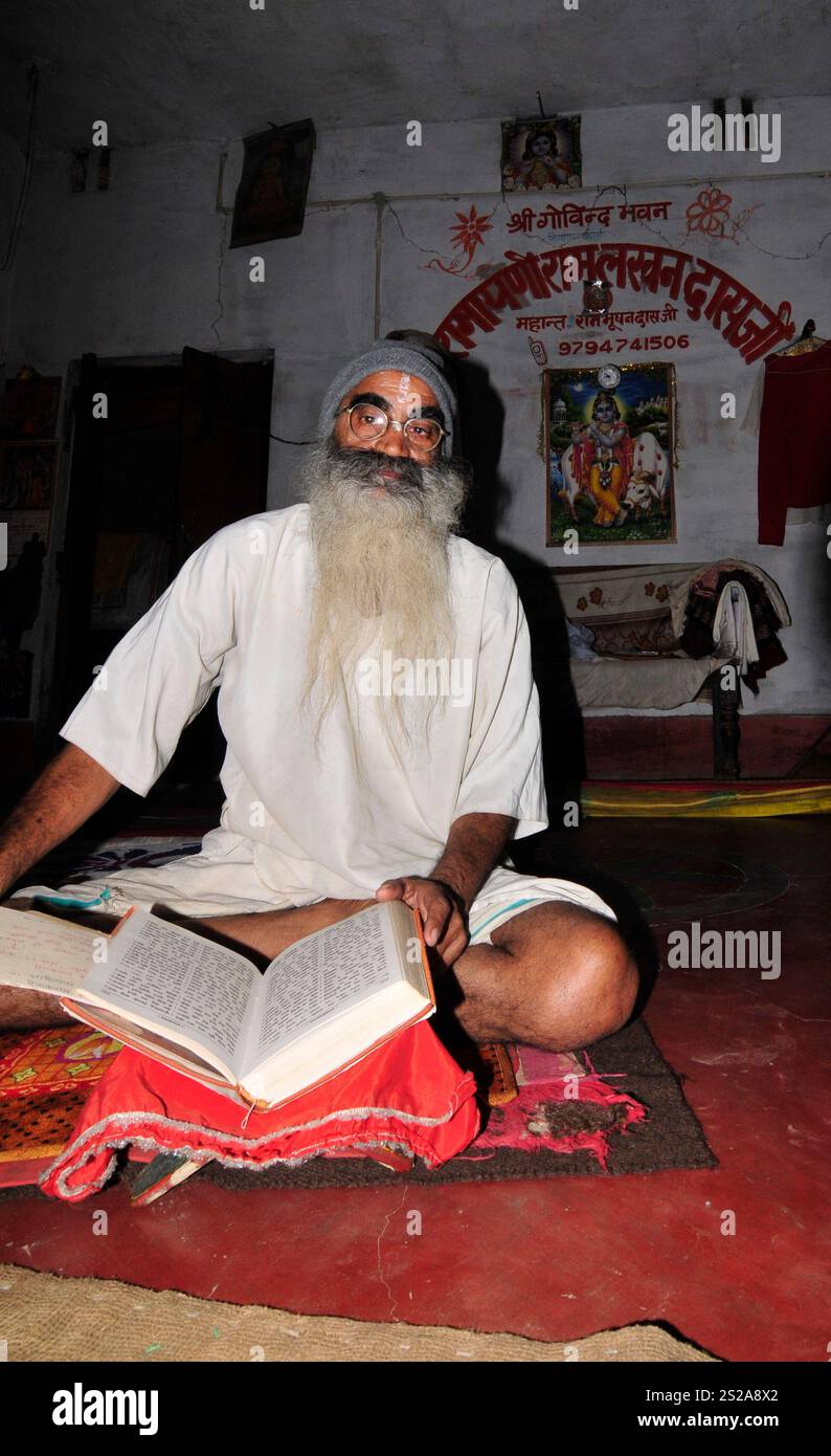 A priest sitting at a small Hindu temple and reading from a holy book ...