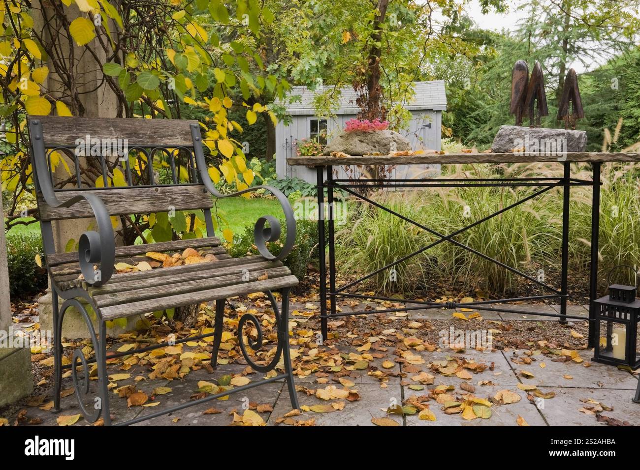 Wood and metal chair, table and fallen leaves on flagstones underneath ...