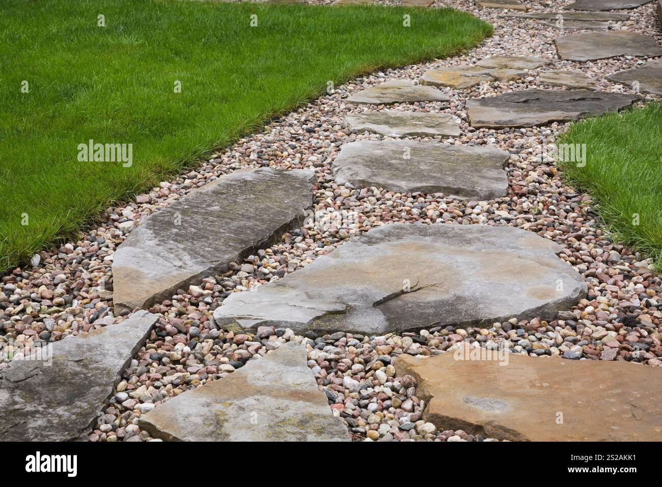 Close-up of flagstone and gravel path through manicured green grass ...
