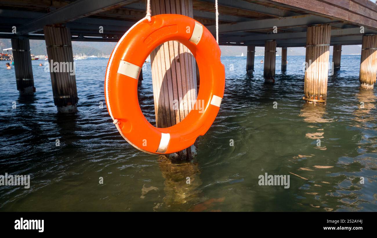 Closeup photo of orange life saving ring hanging on wooden pier at sea ...
