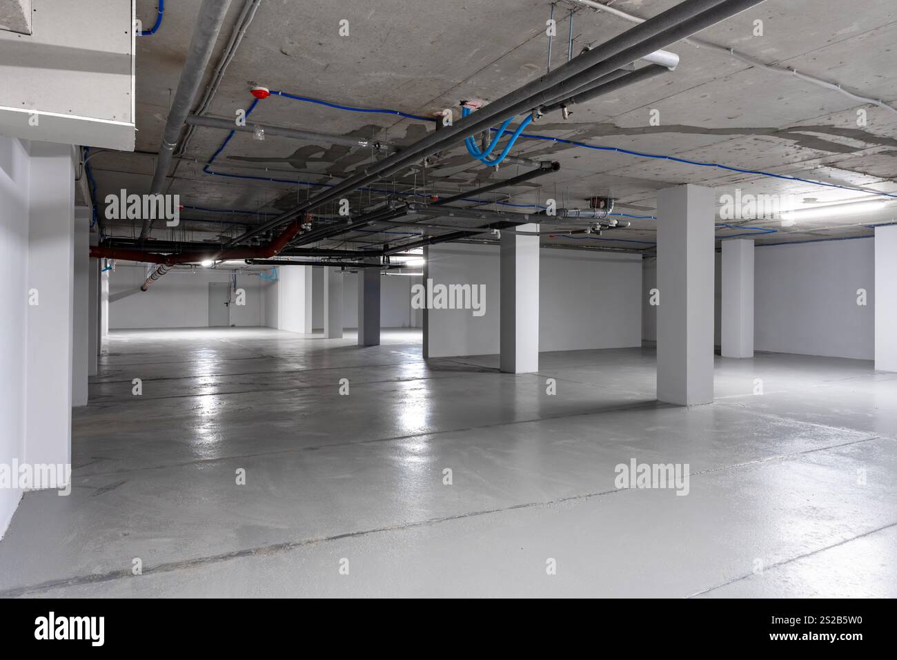 Empty underground parking garage with exposed pipes and clean concrete ...