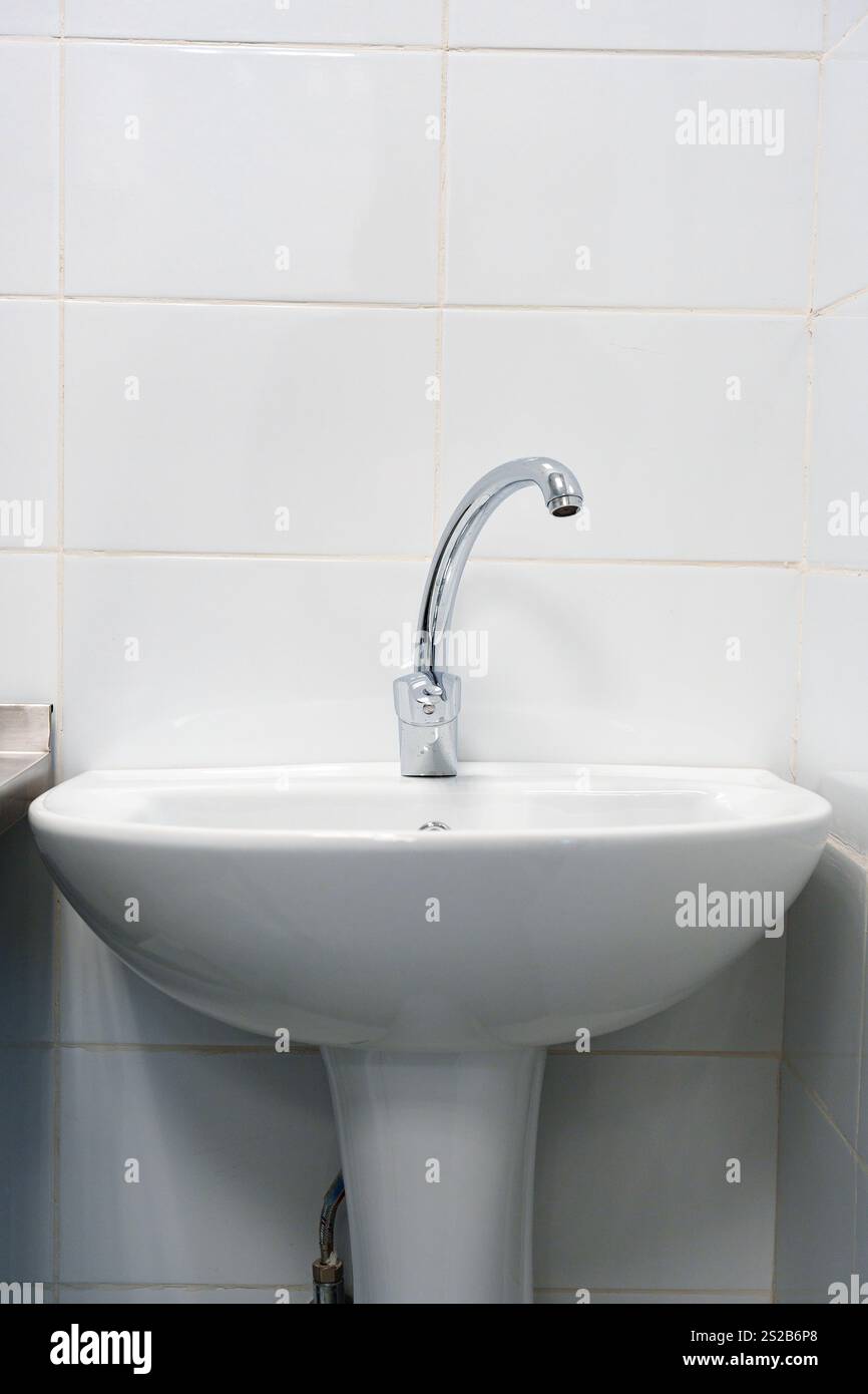 Clean bathroom sink with modern faucet in white-tiled restroom space ...