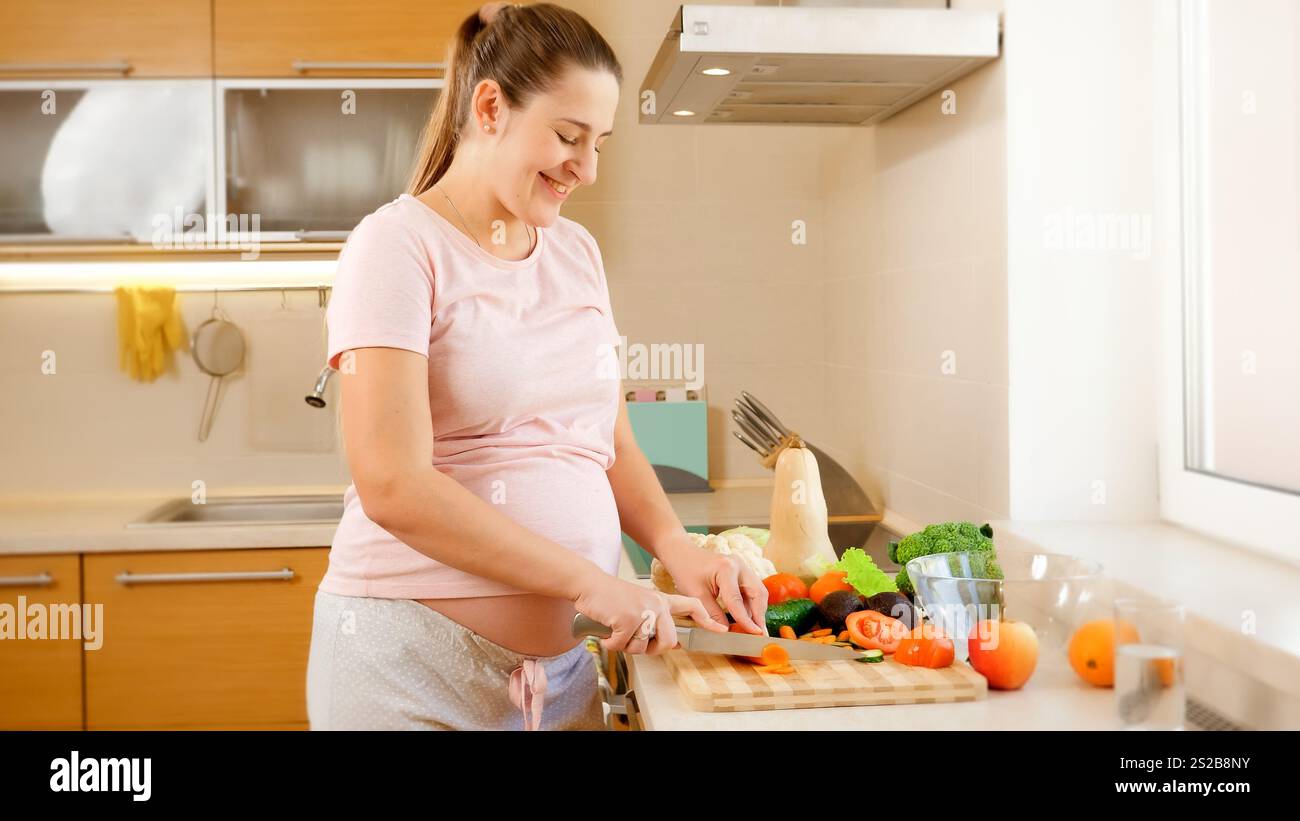 Smiling young woman waiting for baby cooking on kitchen and doing ...
