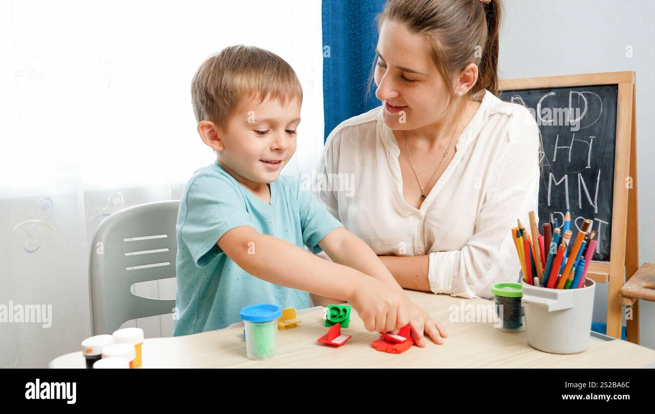 Happy smiling little boy playing with stamps and colorful clay with ...