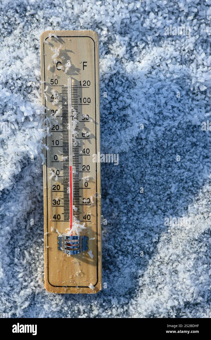 Wooden thermometer lying on a frozen surface covered with ice crystals, indicating freezing ...