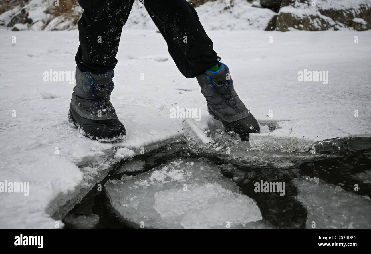 kid wearing winter boots breaking thin ice next to river during ...