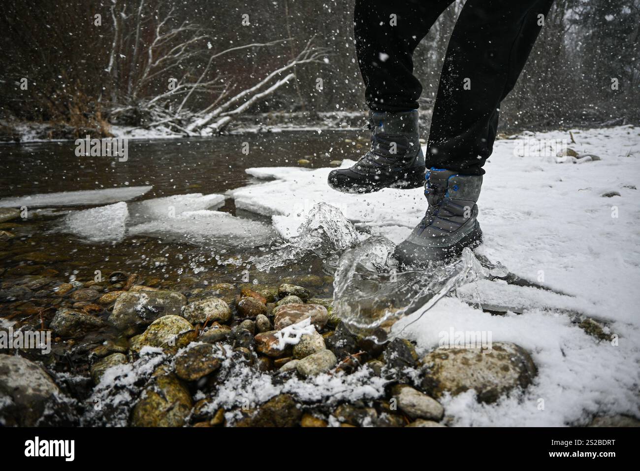 kid wearing winter boots breaking thin ice next to river during ...