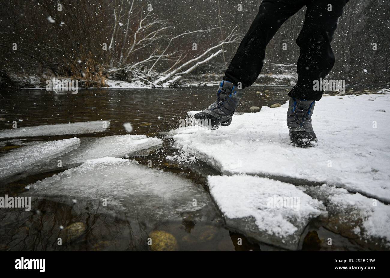 kid wearing winter boots breaking thin ice next to river during ...