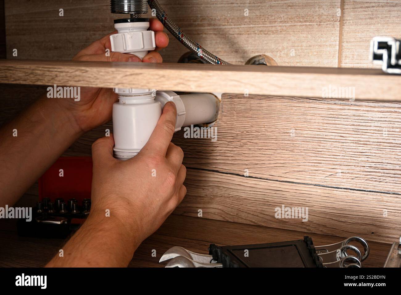 Plumber working on sink drain pipe installation in bathroom, using pvc pipes and connectors ...