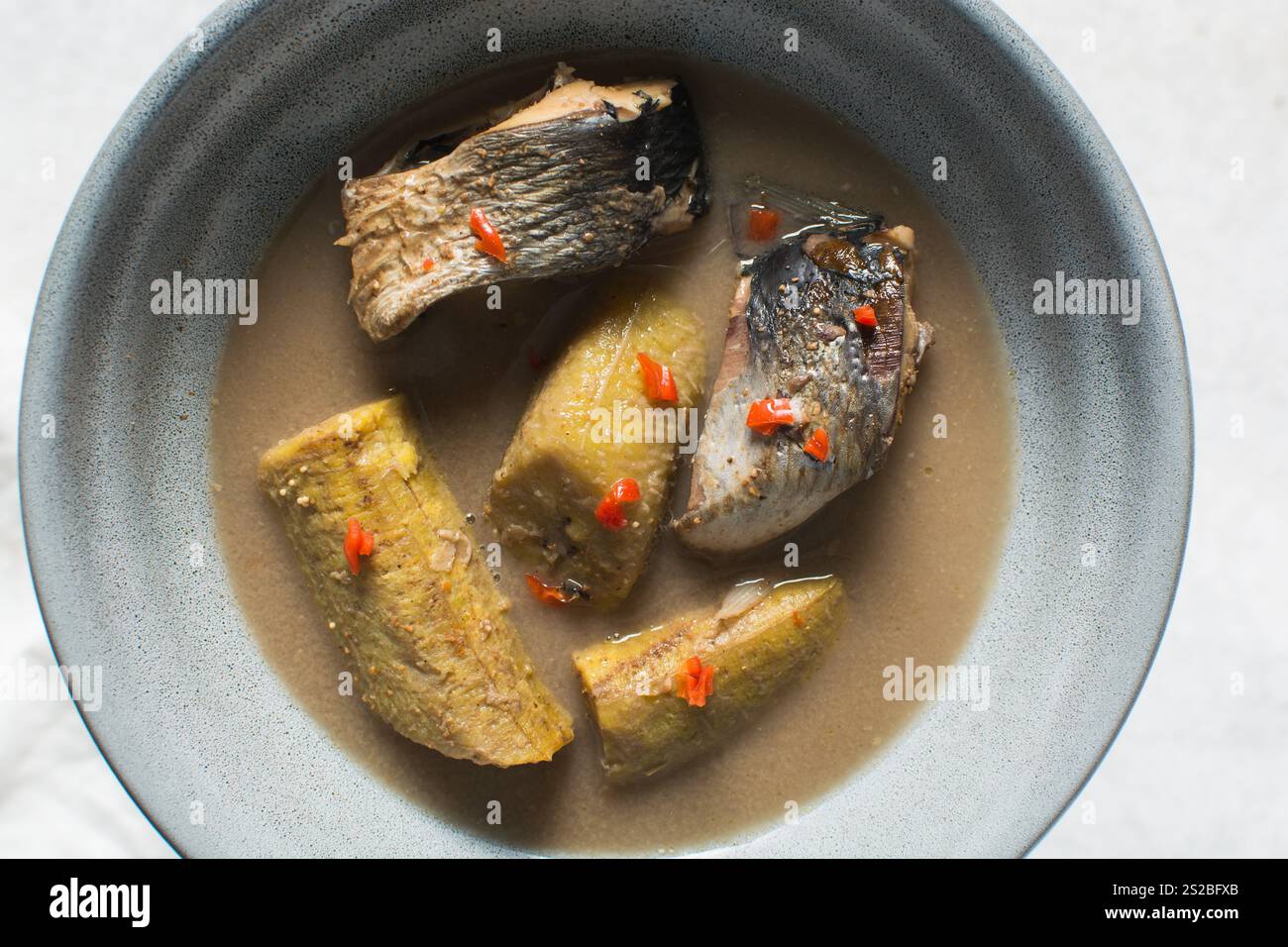 Overhead view of Nigerian pepper soup with fish and plantain in a white ...