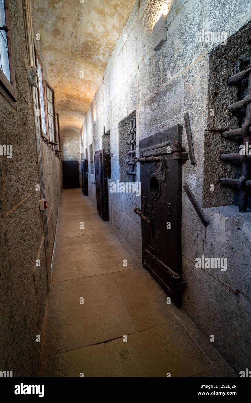A narrow, dimly lit stone corridor lined with heavy iron prison doors ...